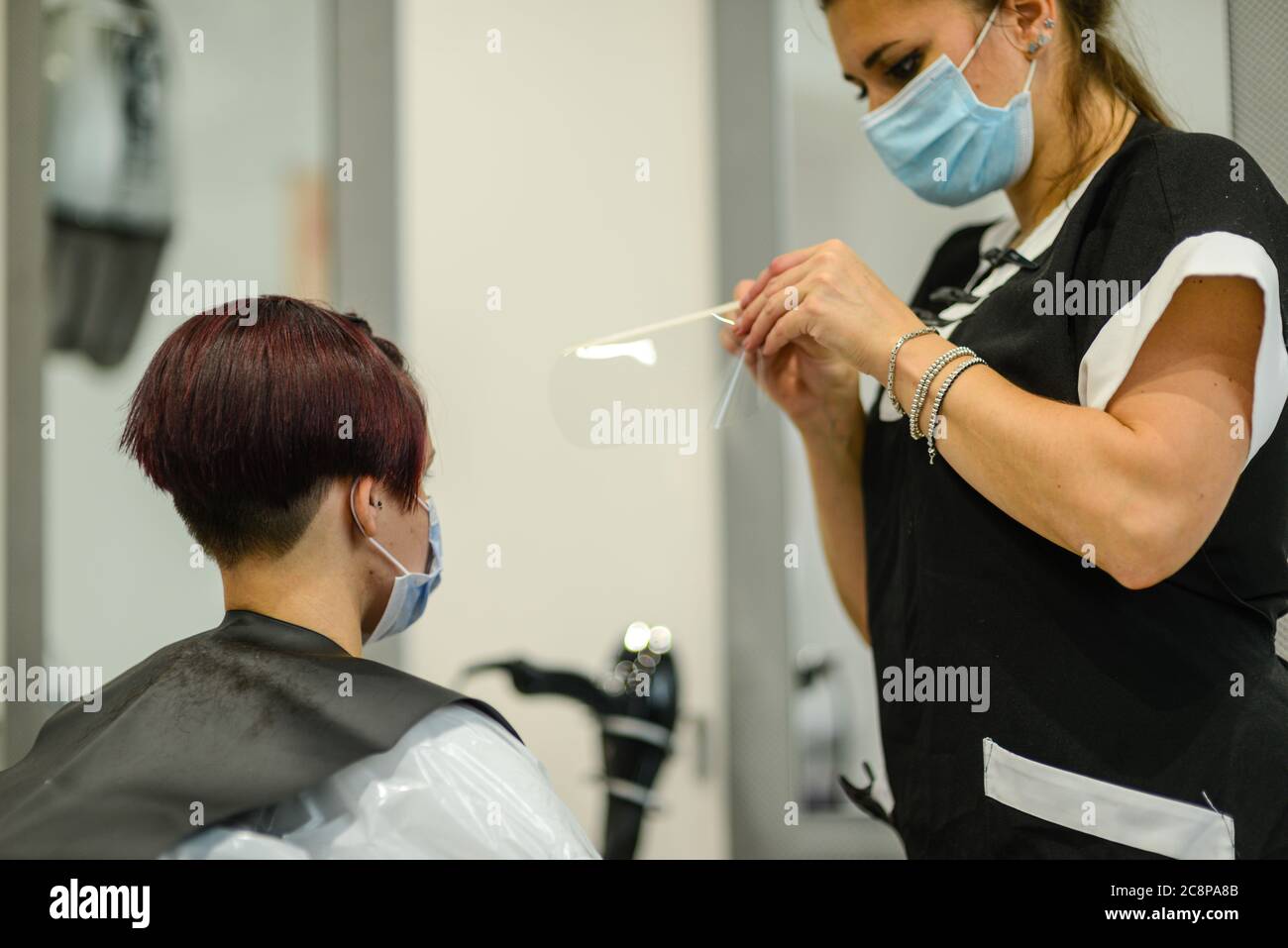 Female hair stylist wearing face mask puting a protective face visor to ...