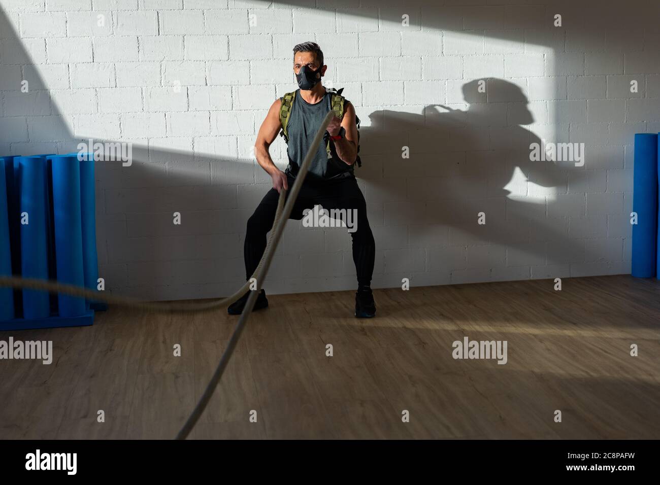 Sportsman at rope workout with training mask. Indoor on oak floor with ...