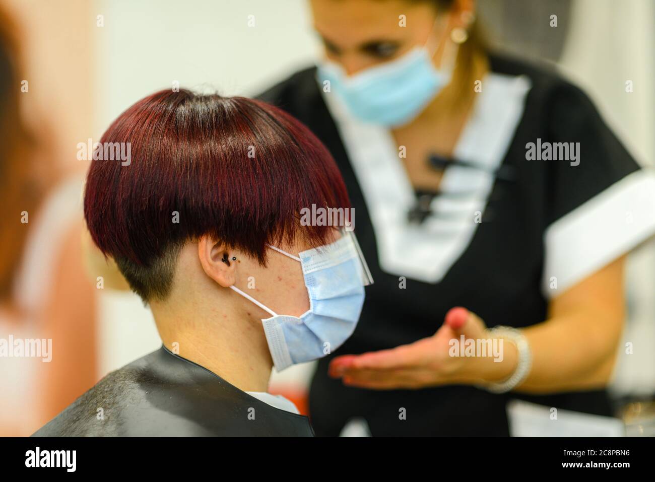 Female hair stylist wearing face mask styling a short red haired ...