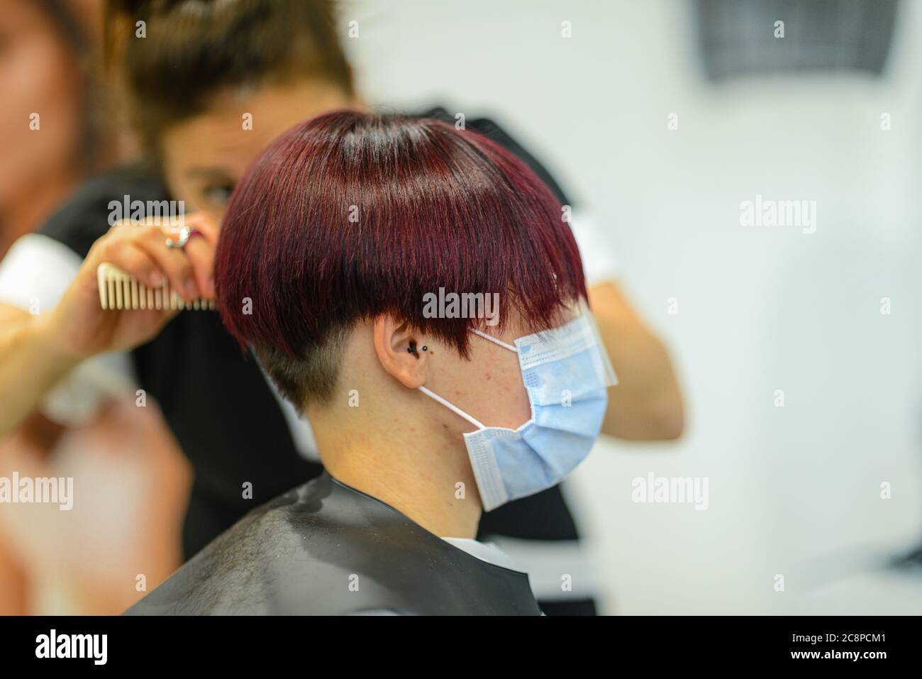 Female hair stylist wearing face mask styling a short red haired ...