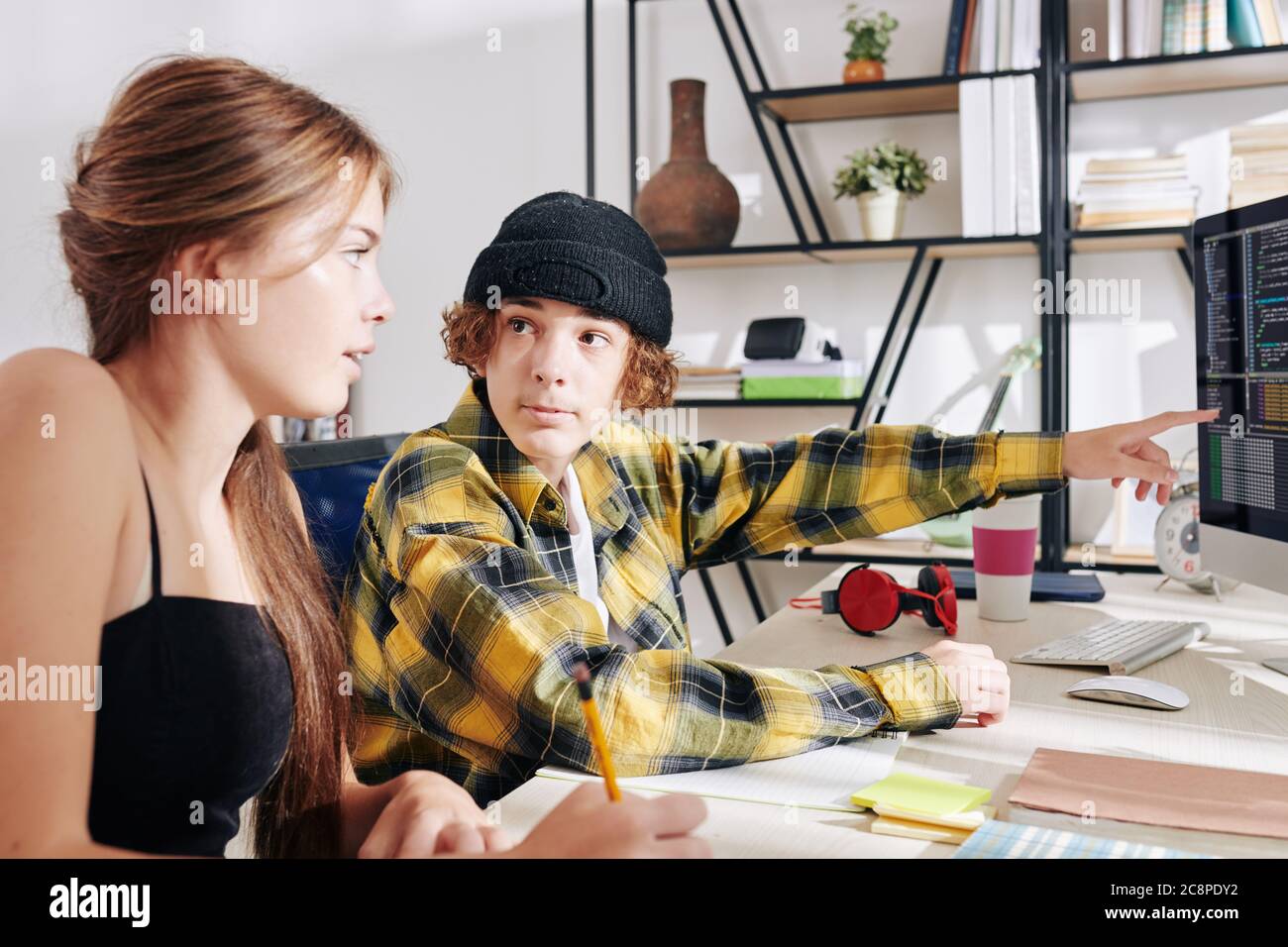 Teenage boy in plaid shirt and hat pointing at computer screen with ...