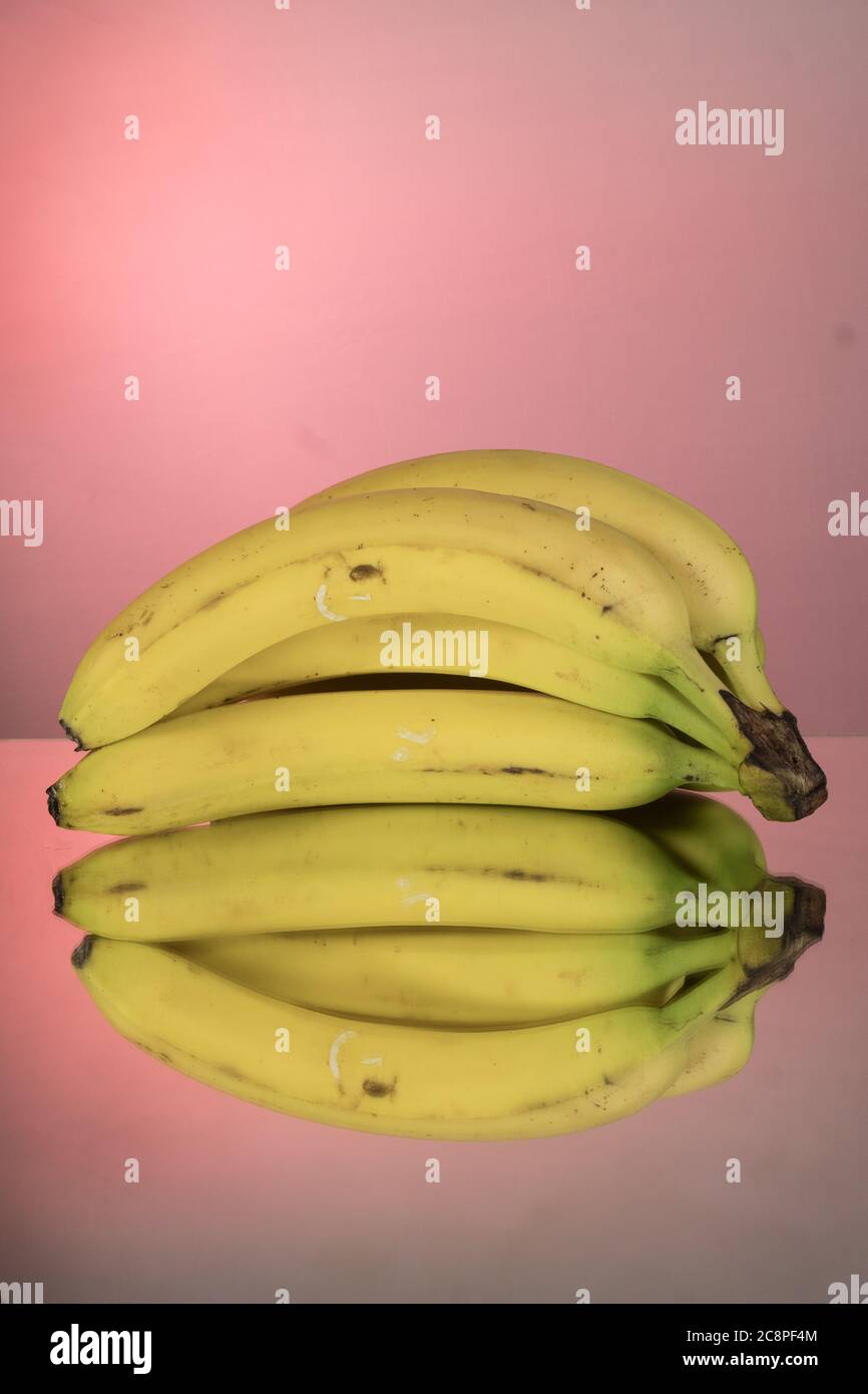 A bunch of bananas on mirroring table on mirror red background with ...