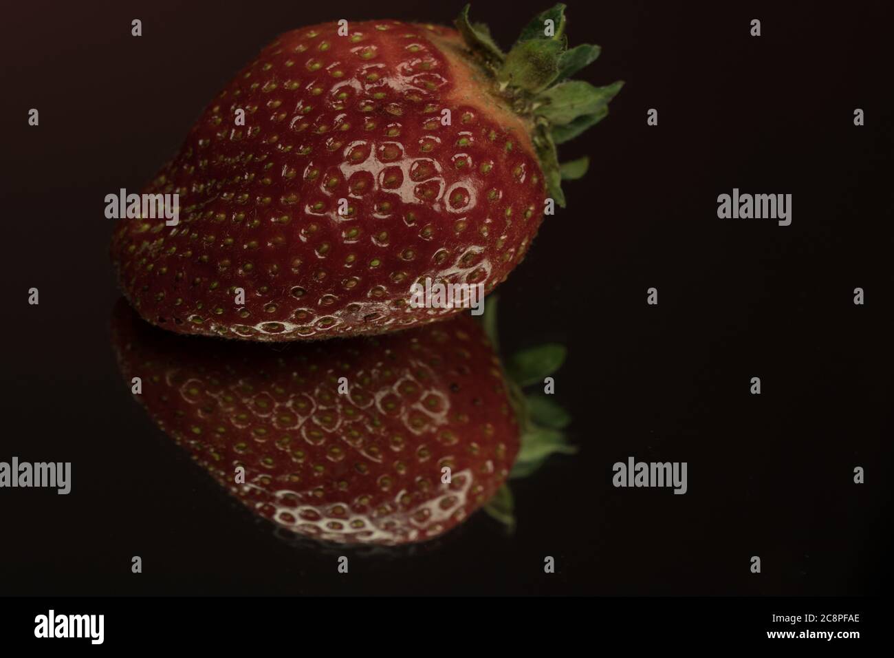 A tasty red ripe strawberry on a mirror. Isolated close-up detail shot ...