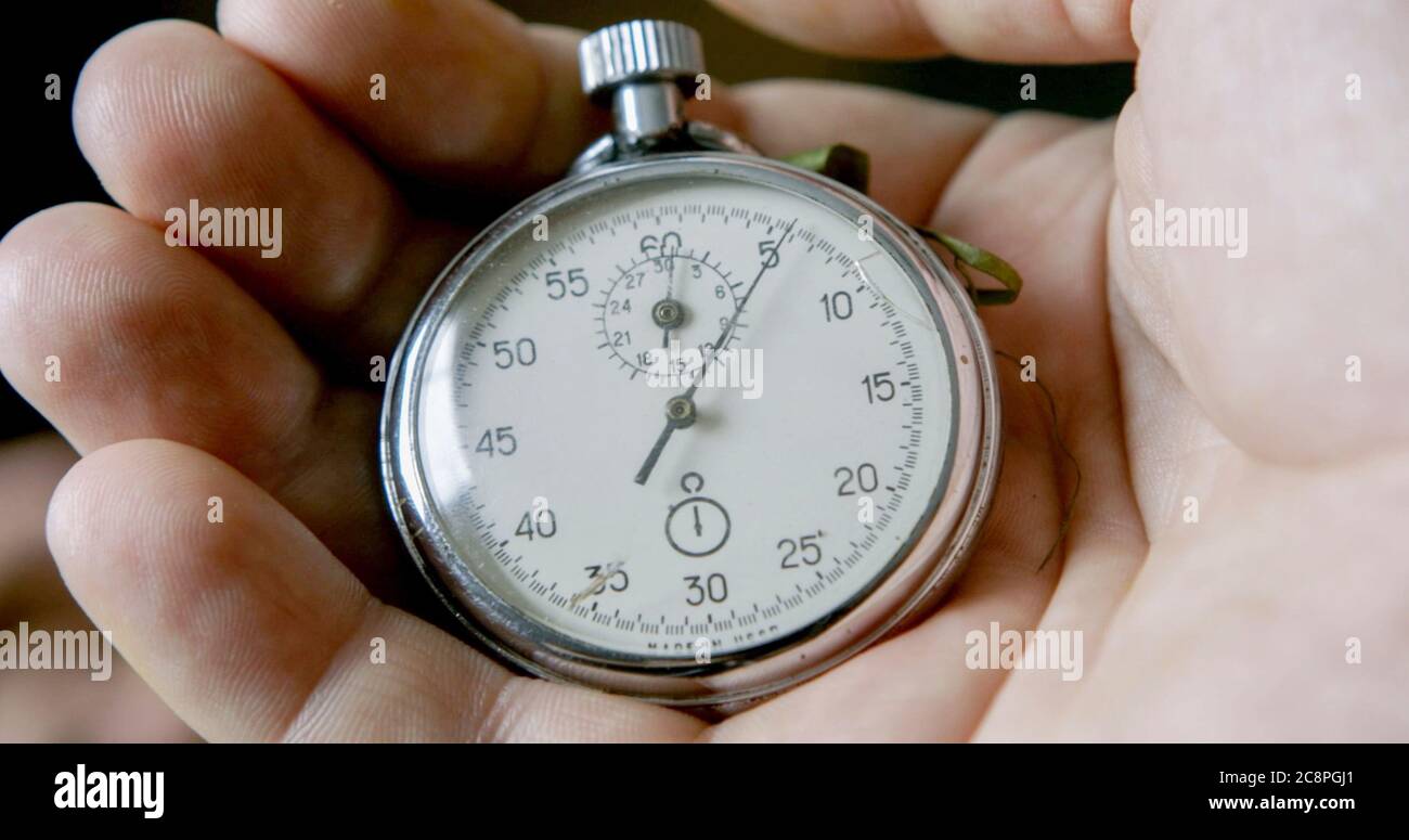 Male hand holding stopwatch on dark background Stock Photo - Alamy