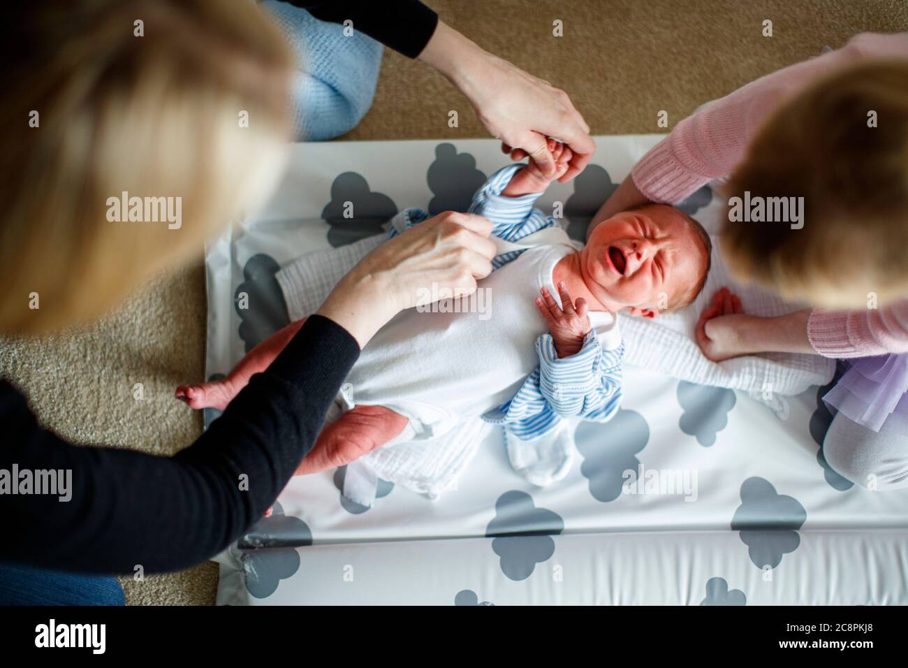 Mother and daugher tending to crying baby on changing mat Stock Photo ...