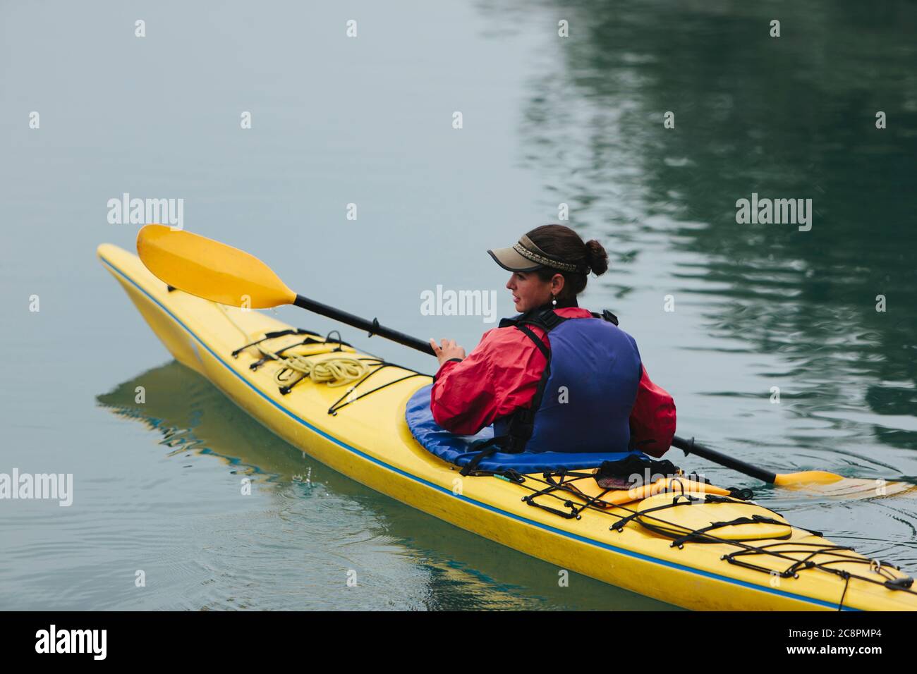 Female sea kayaker paddling pristine waters of Muir Inlet, overcast sky ...