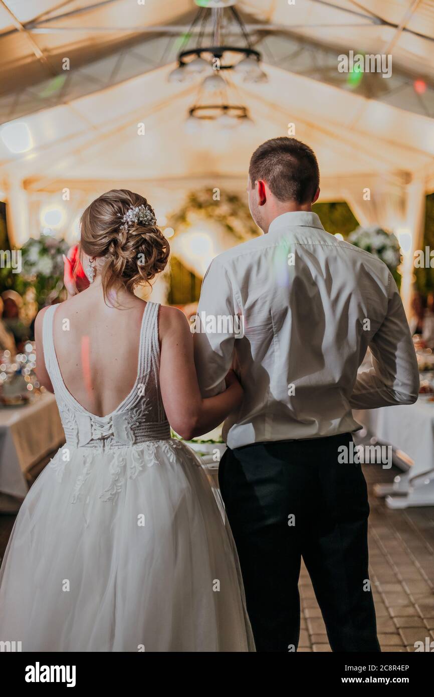Back view of romantic couple of bride and groom on banquet hand in hand ...