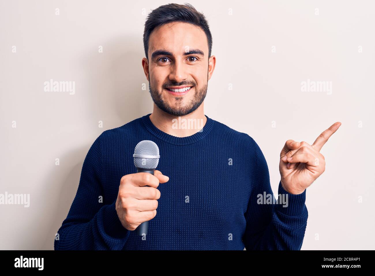 Young handsome singer man with beard singing song using microphone over white background smiling ...