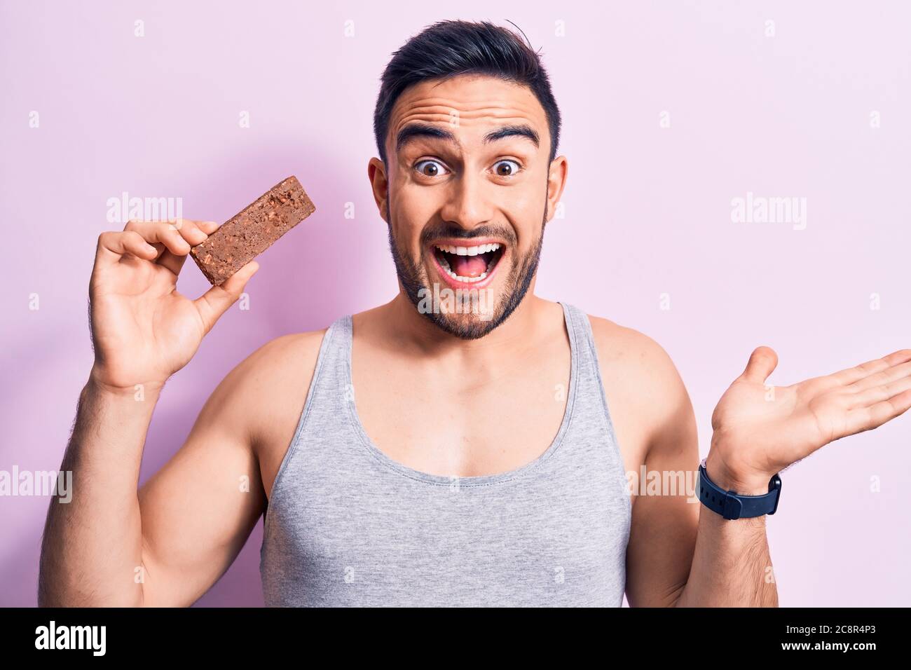 Young handsome man with beard eating energy protein bar over isolated ...