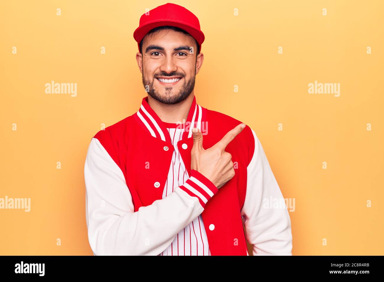 Handsome sporty man with beard wearing baseball jacket and cap over ...