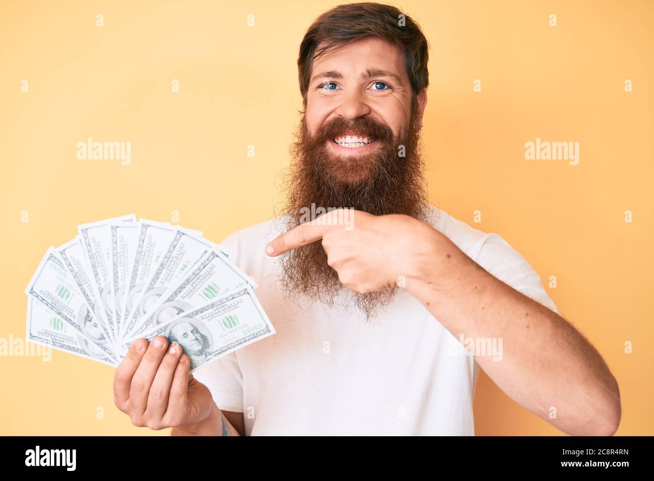 Handsome young red head man with long beard holding dollars smiling ...