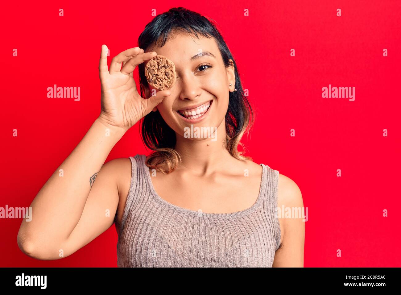 Young woman holding cookie looking positive and happy standing and ...