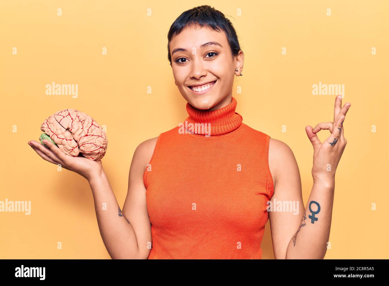 Young woman holding brain doing ok sign with fingers, smiling friendly ...