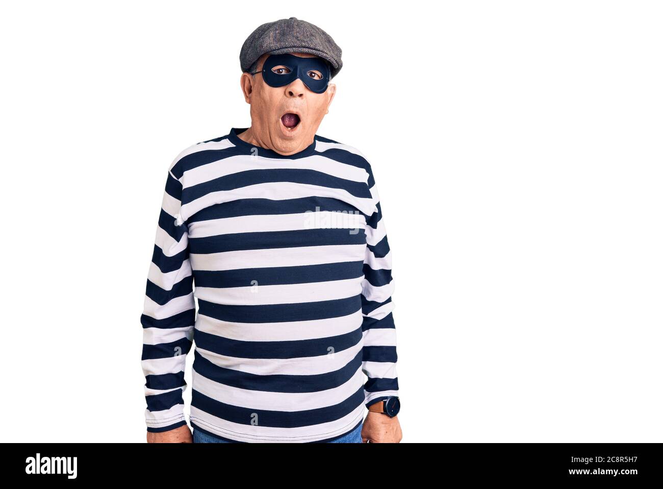 Senior handsome man wearing burglar mask and t-shirt in shock face ...