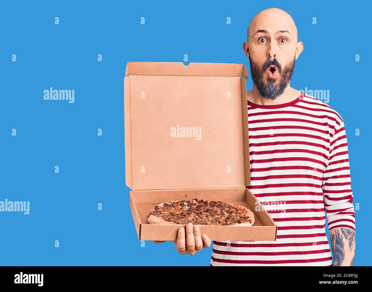 Young handsome man holding delivery pizza box scared and amazed with ...