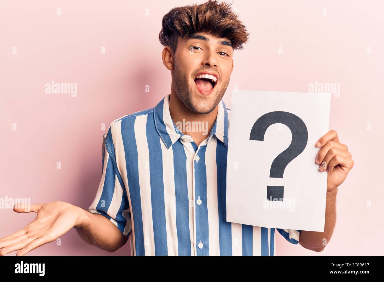Young hispanic man holding question mark celebrating achievement with ...