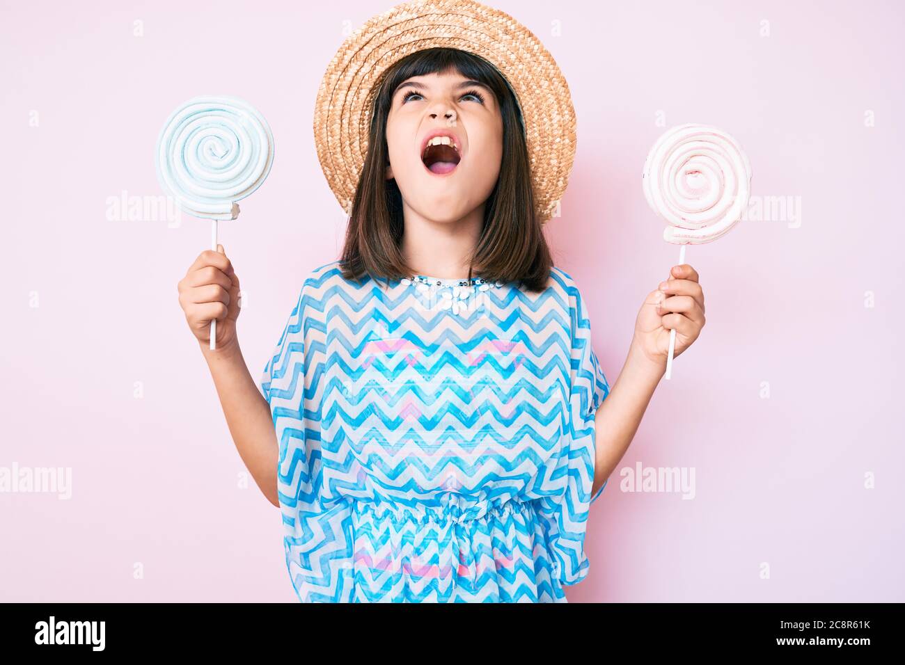 Young little girl with bang wearing summer dress eating candy angry and ...
