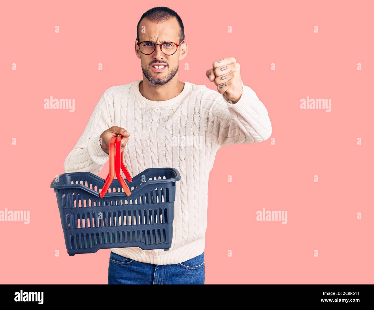 Young handsome man holding supermarket shopping basket annoyed and ...