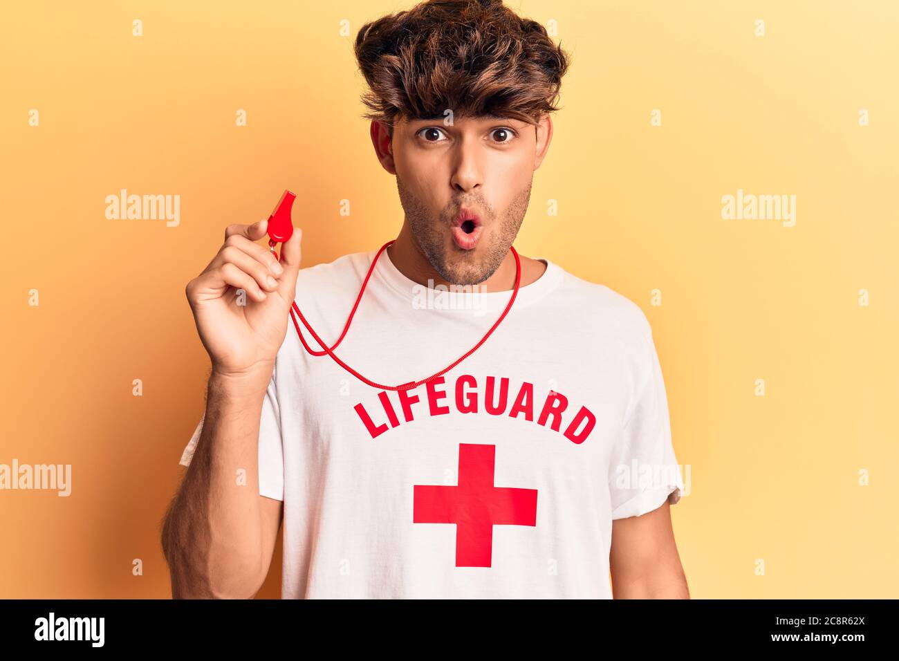 Young hispanic man wearing lifeguard t shirt holding whistle scared and ...