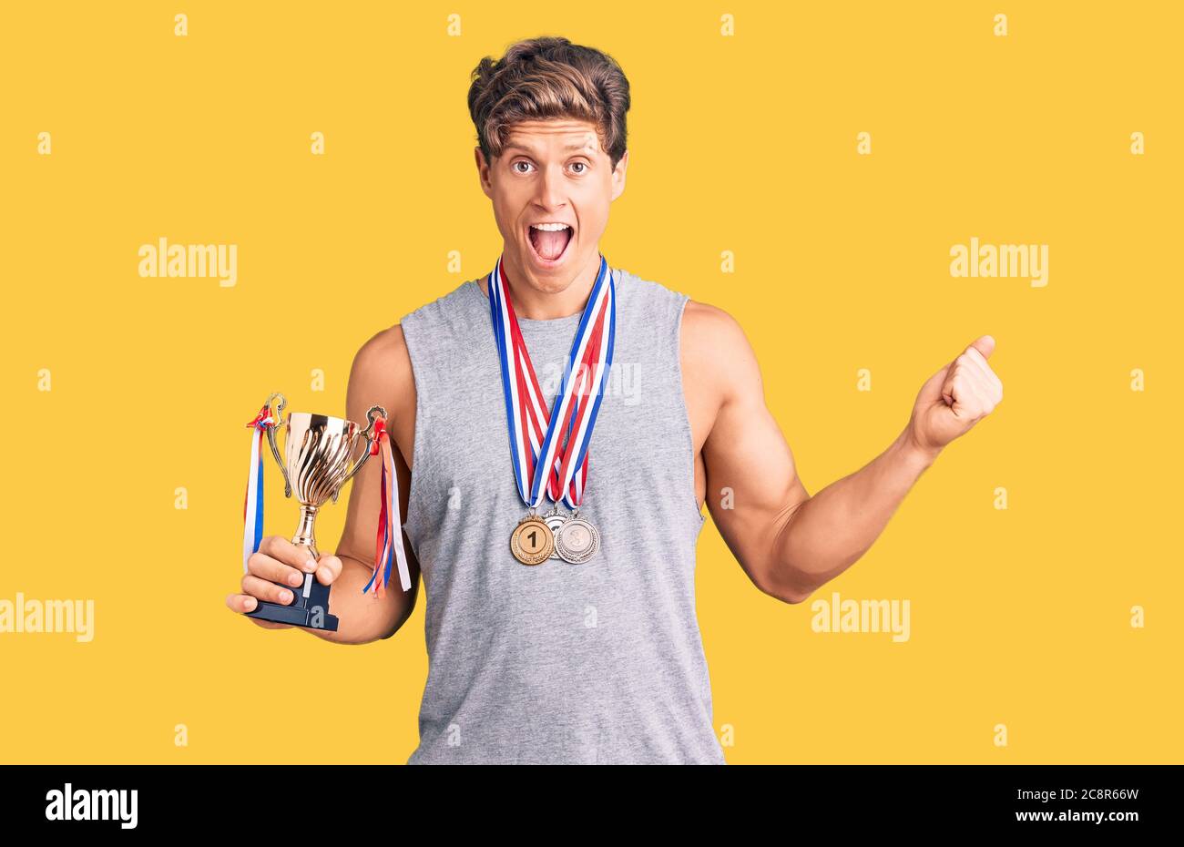 Young handsome man holding champion trophy wearing medals screaming ...