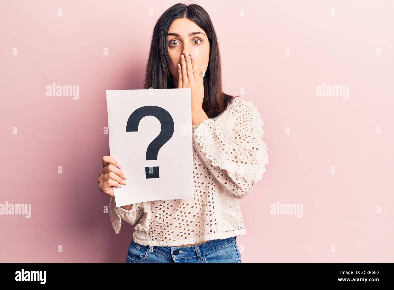 Young beautiful girl holding question mark covering mouth with hand ...
