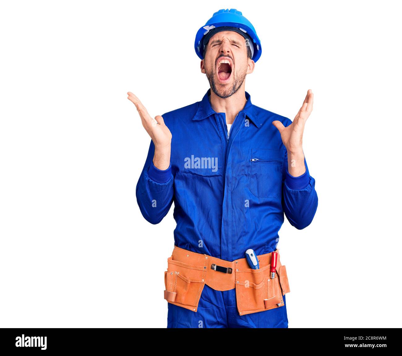 Young handsome man wearing worker uniform and hardhat celebrating mad ...