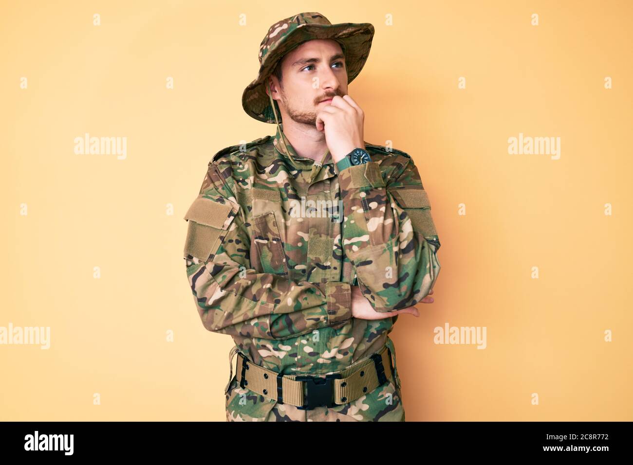 Young caucasian man wearing camouflage army uniform with hand on chin ...