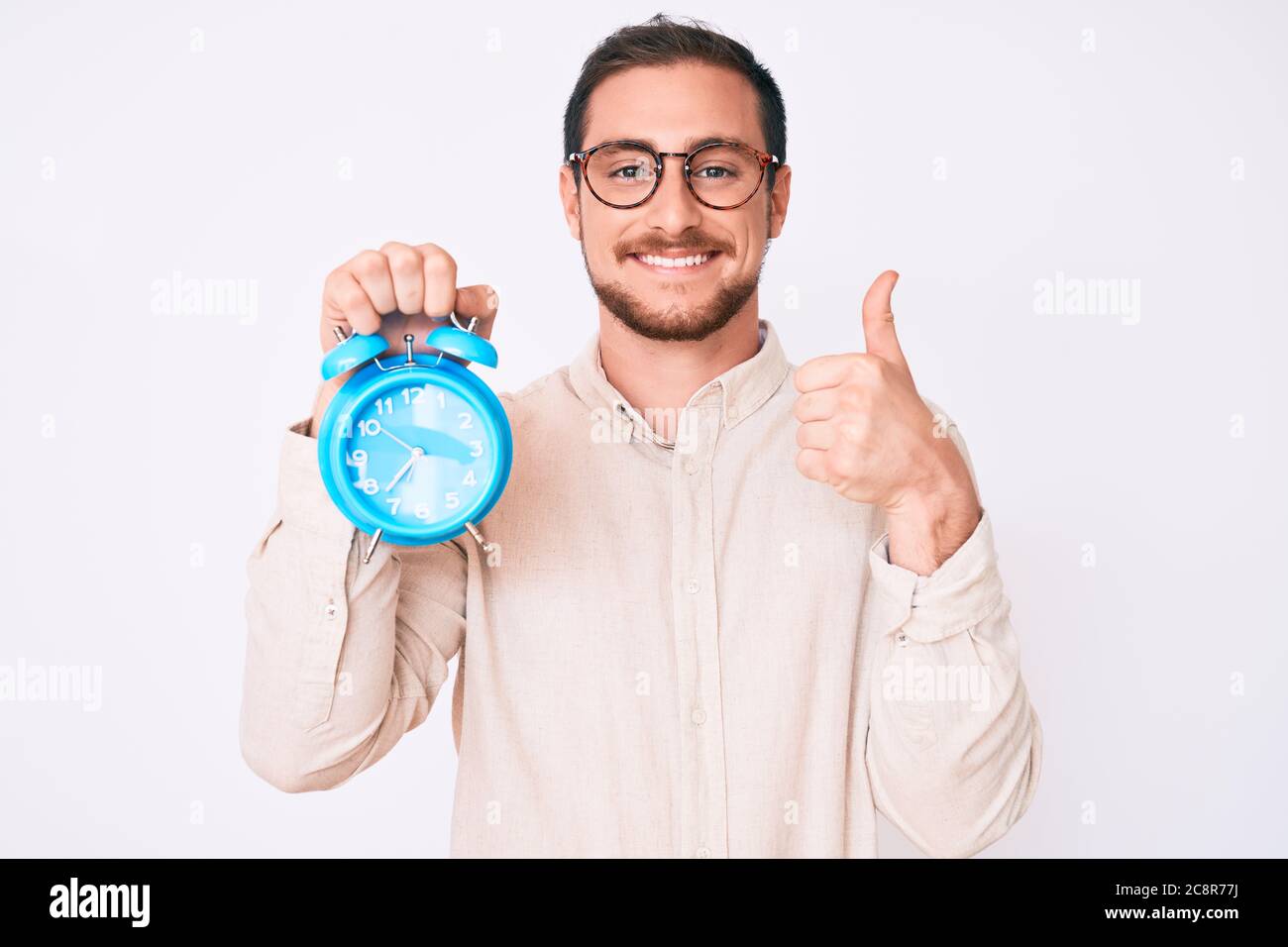 Young handsome man holding alarm clock smiling happy and positive ...
