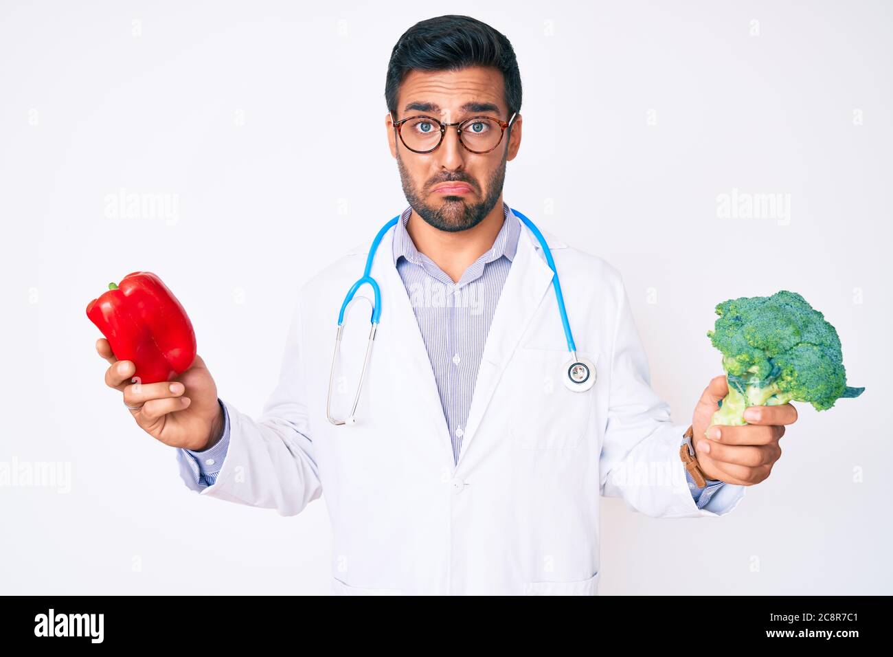 Young hispanic man wearing doctor stethoscope holding red pepper and ...