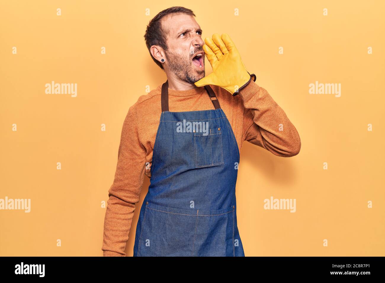 Young handsome man wearing gardener apron and gloves shouting and ...