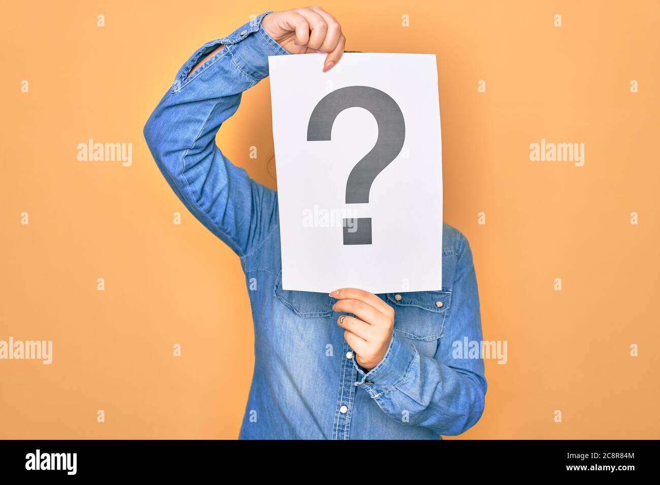 Woman covering face holding paper with question mark symbol. Standing ...