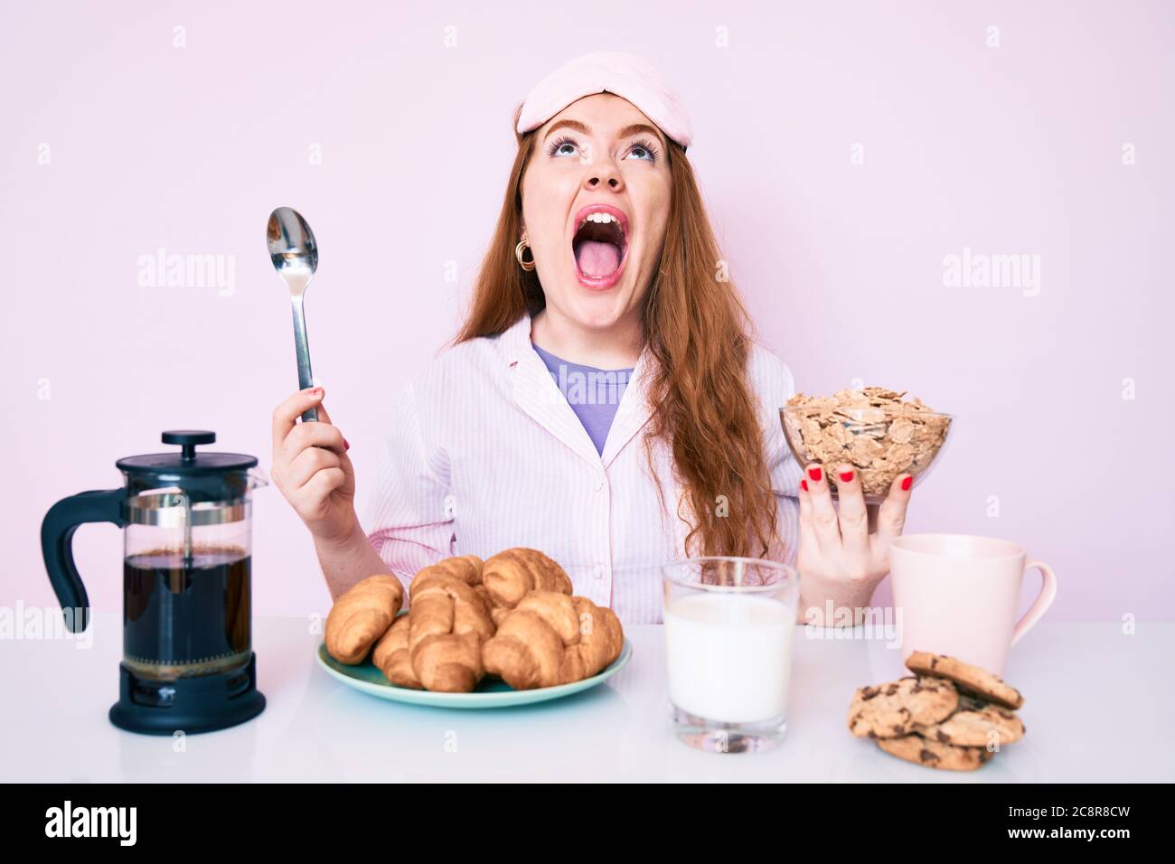 Young beautiful redhead woman sitting on the table having breakfast ...