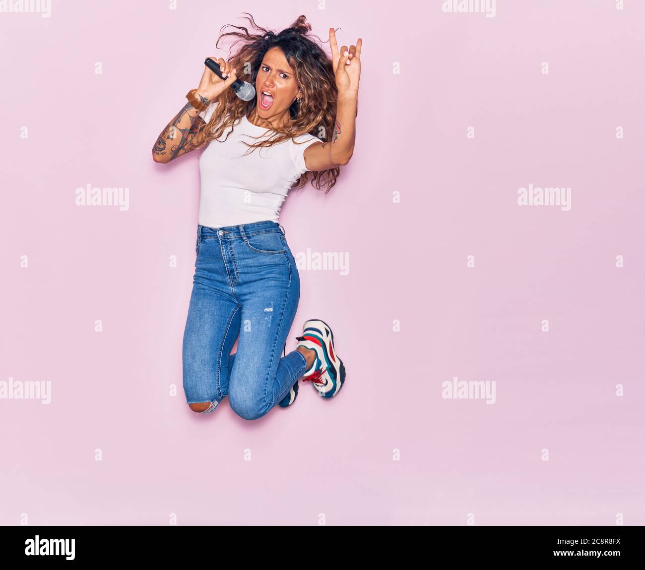 Young beautiful curly singer woman with tattoo smiling happy. Jumping ...