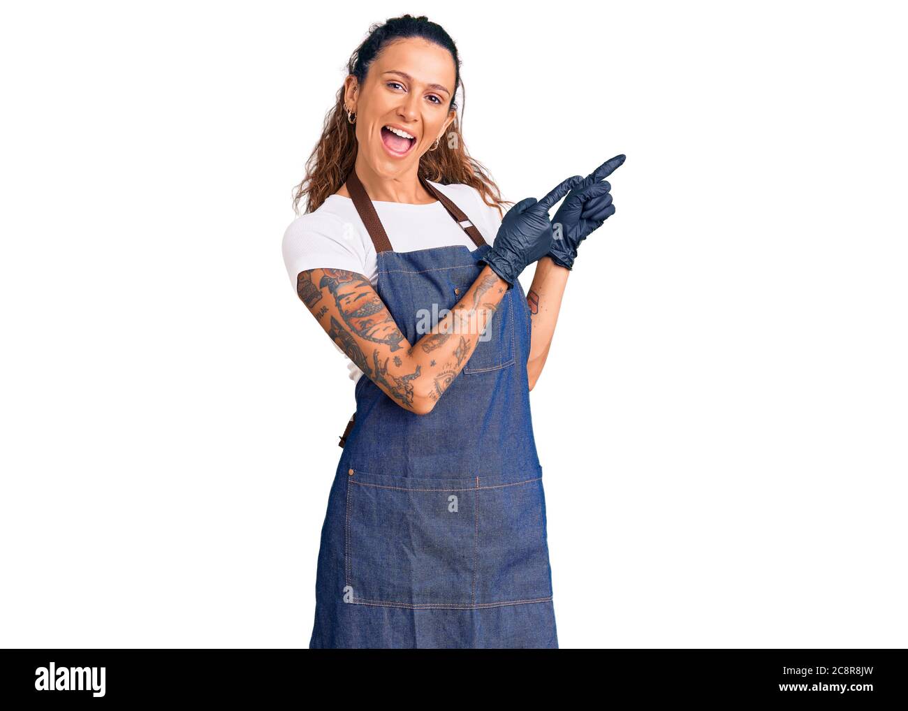 Young hispanic woman with tattoo wearing barber apron and gloves ...