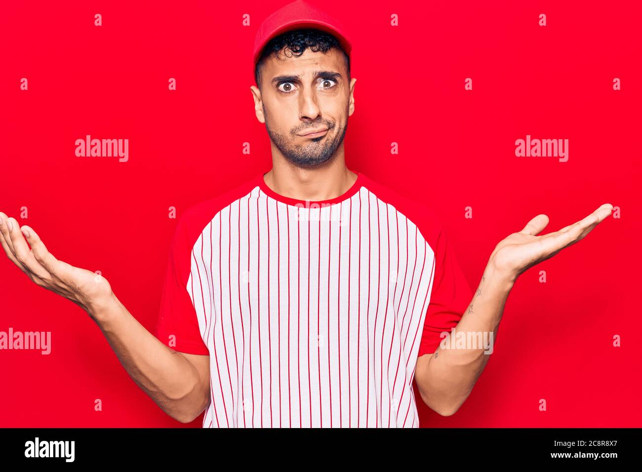 Young hispanic man wearing baseball uniform clueless and confused with ...