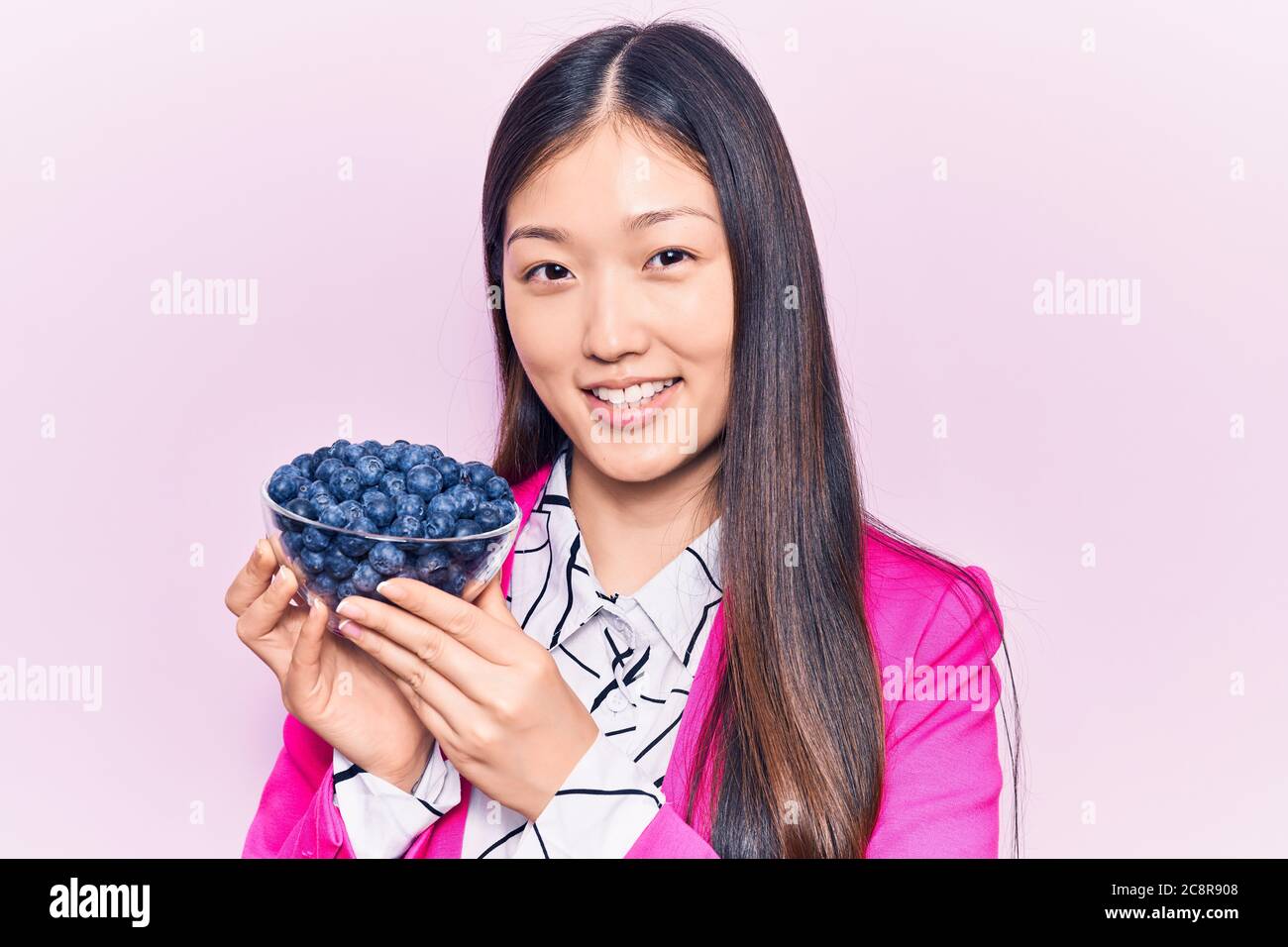 Young beautiful blonde woman holding bowl with blueberries looking ...