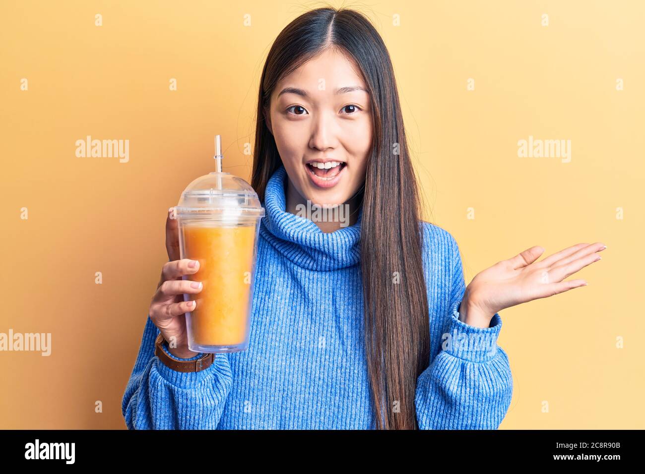 Young beautiful chinese woman drinking glass of orange juice ...
