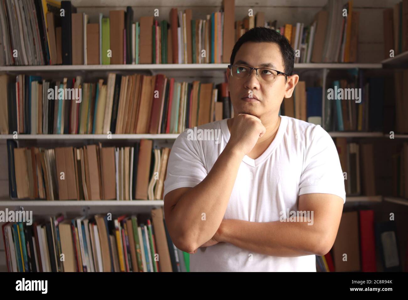 Asian man thinking while standing in front of bookshelf, education ...