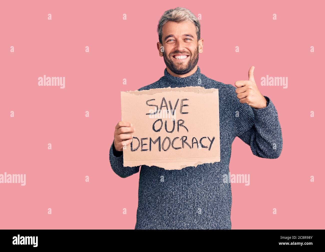 Young blond man holding save our democracy cardboard banner smiling ...