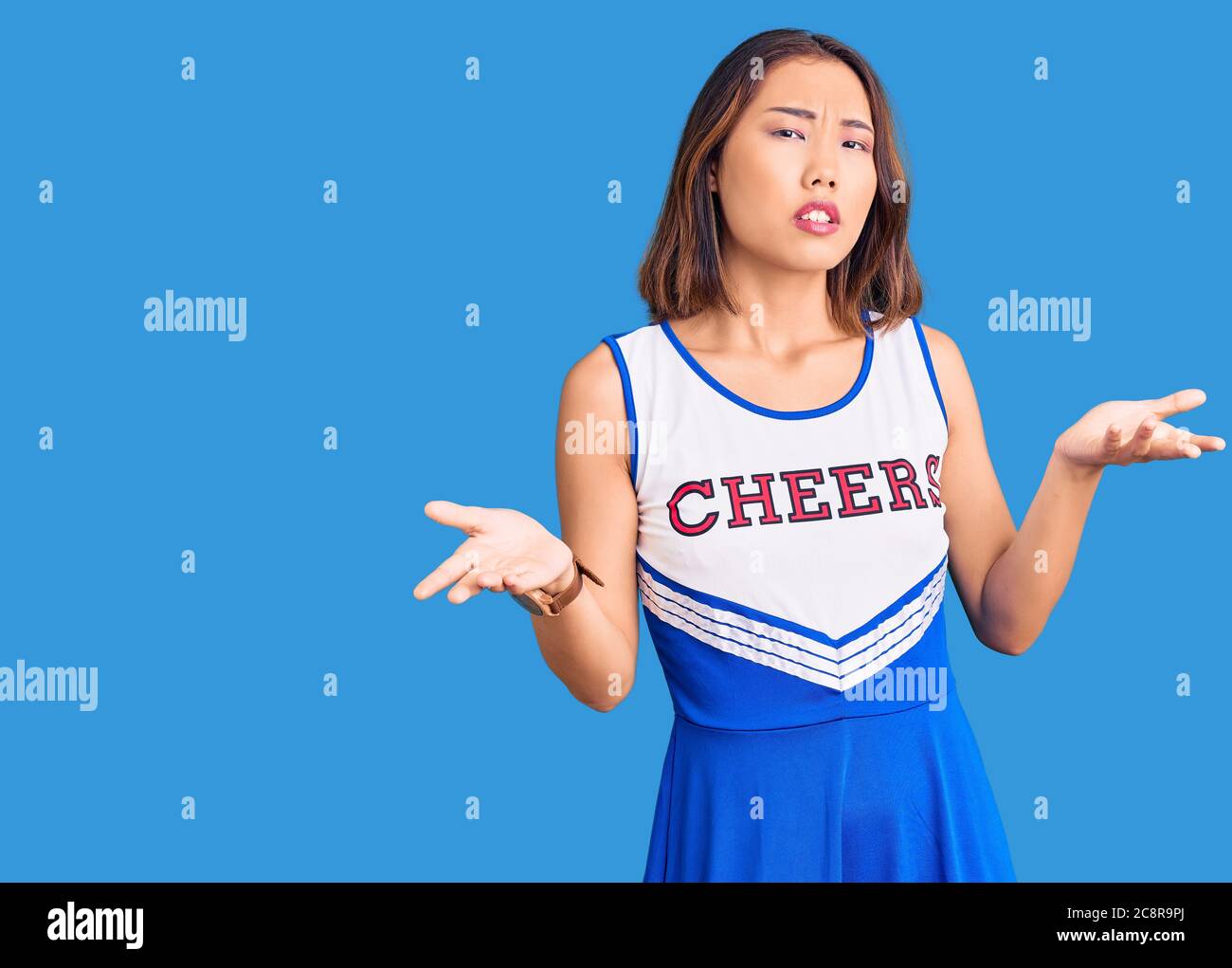 Young beautiful chinese girl wearing cheerleader uniform clueless and ...