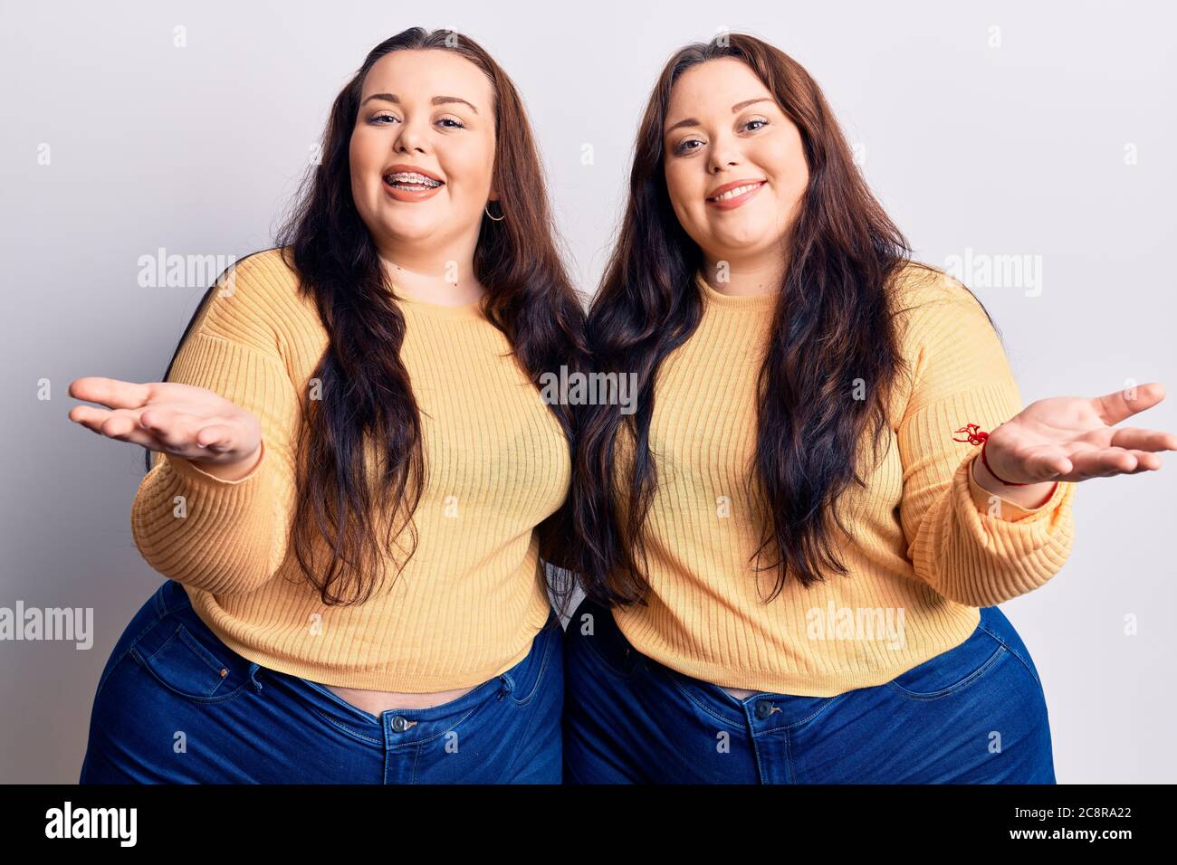 Young plus size twins wearing casual clothes smiling cheerful offering ...