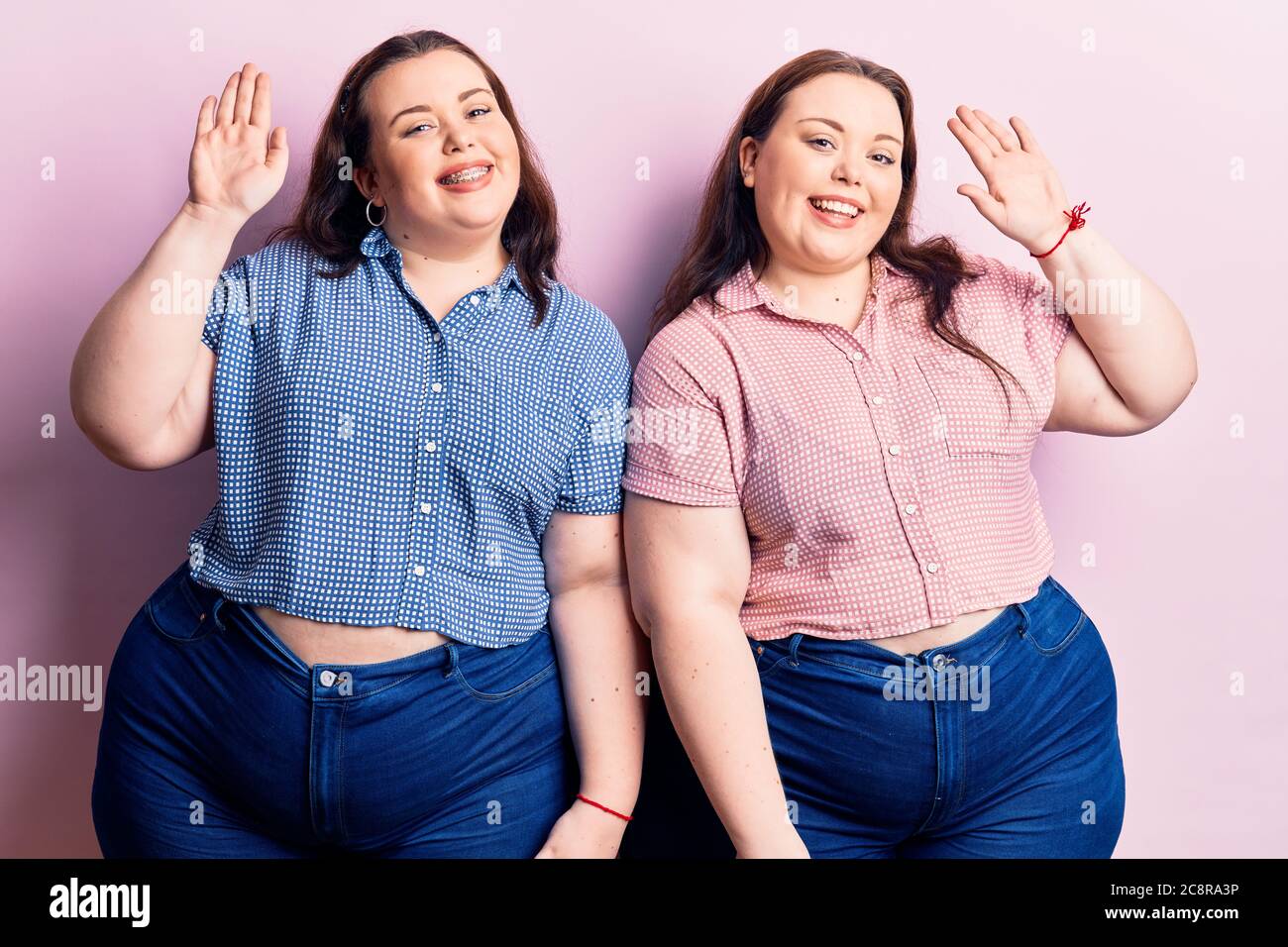 Young plus size twins wearing casual clothes waiving saying hello happy ...