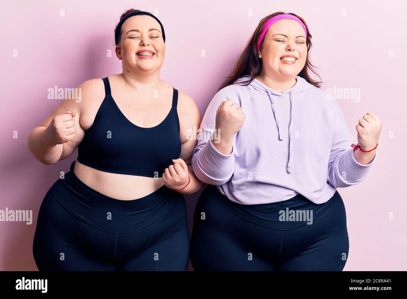 Young plus size twins wearing sportswear excited for success with arms ...