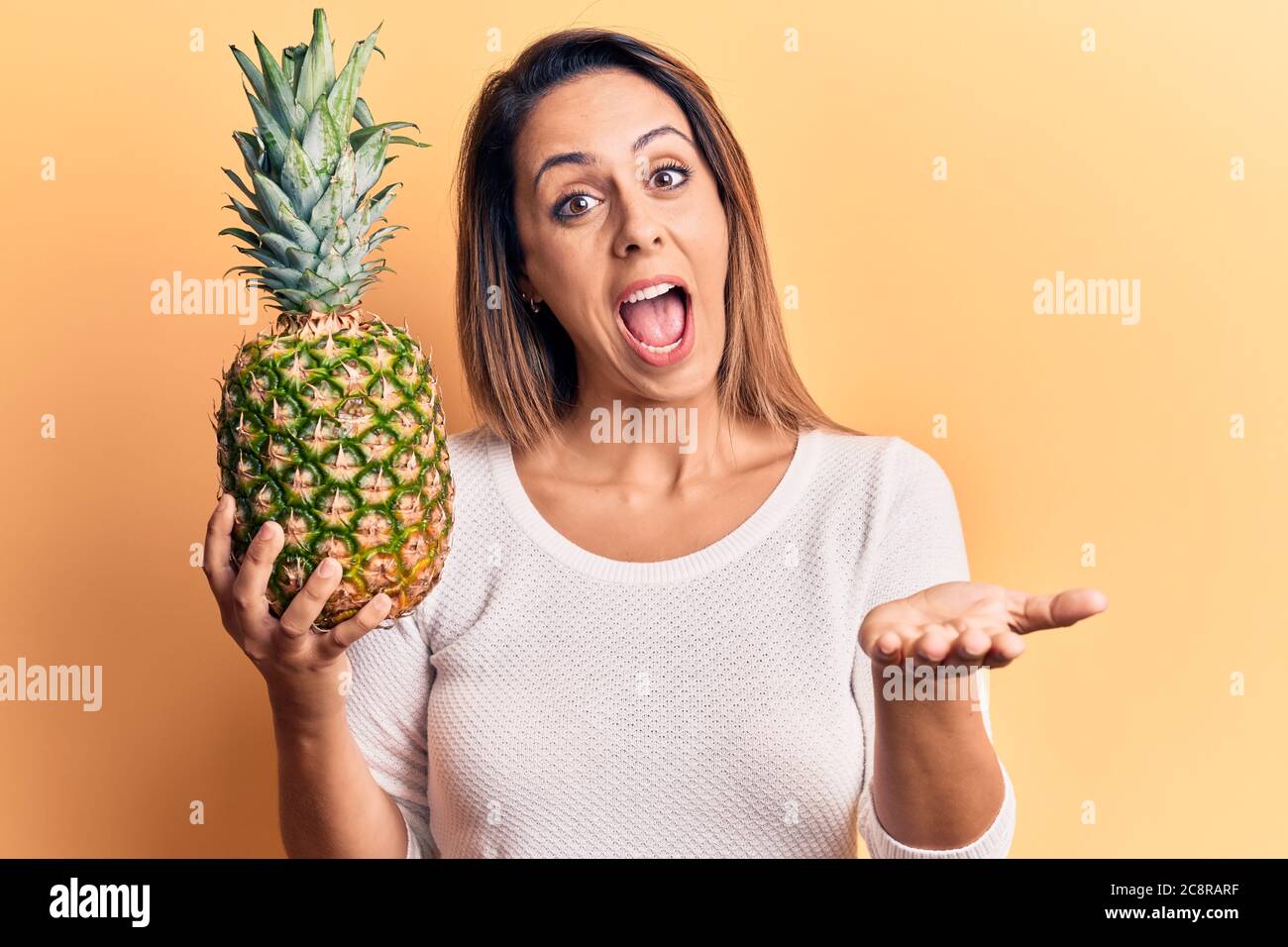 Young beautiful woman holding pineapple celebrating achievement with ...