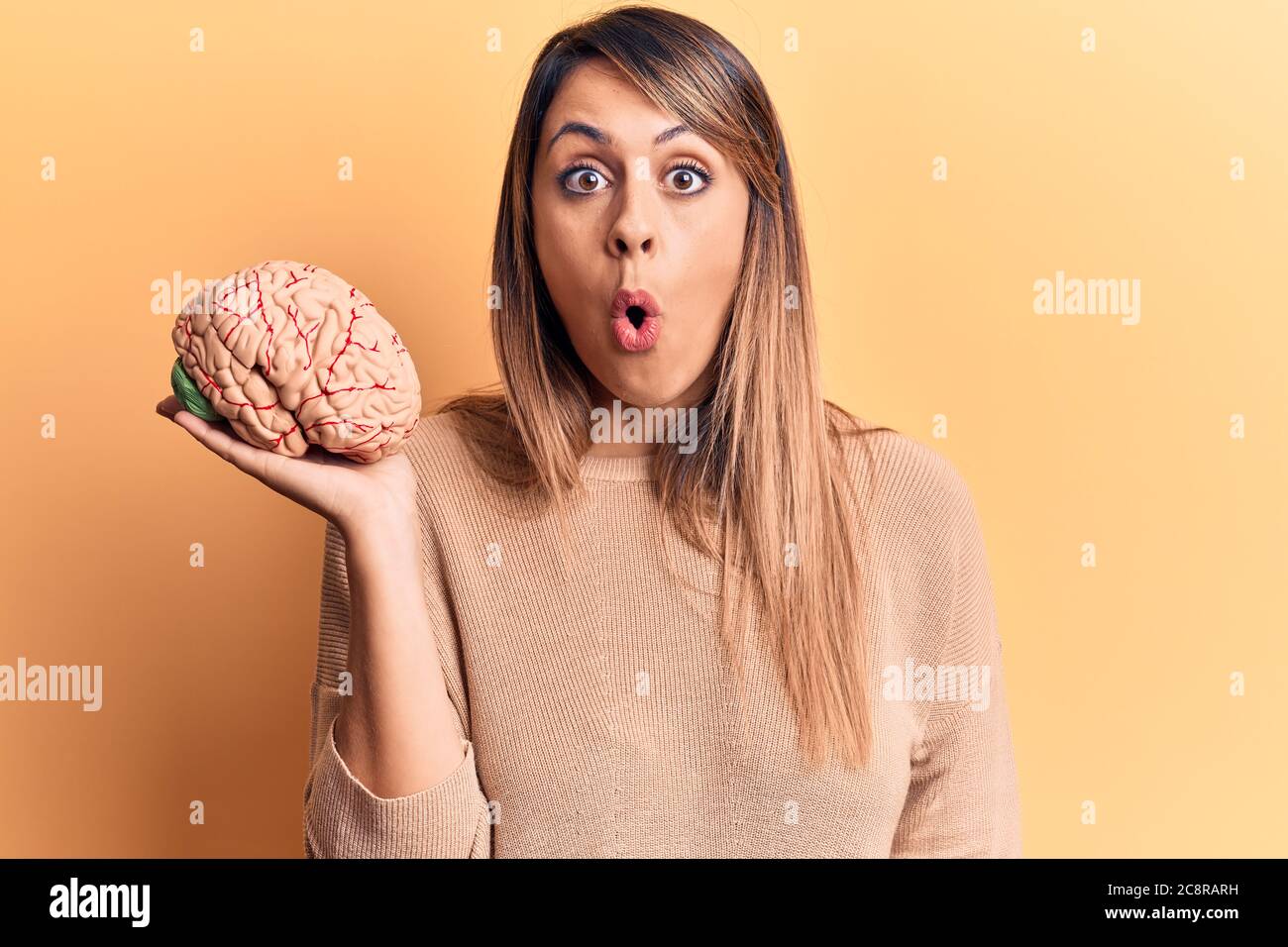 Young beautiful woman holding brain scared and amazed with open mouth ...