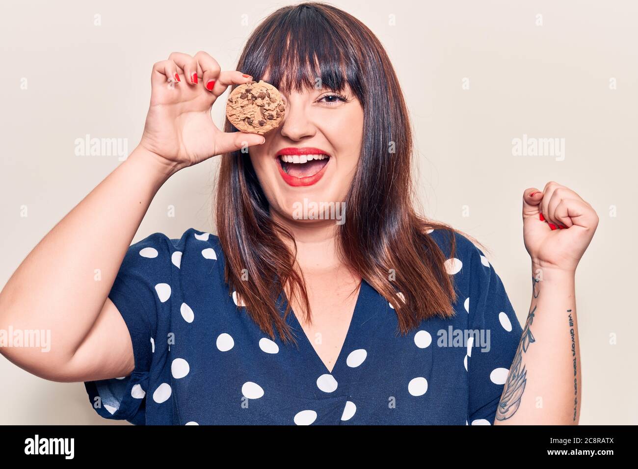 Young plus size woman holding chocolate cookie screaming proud ...