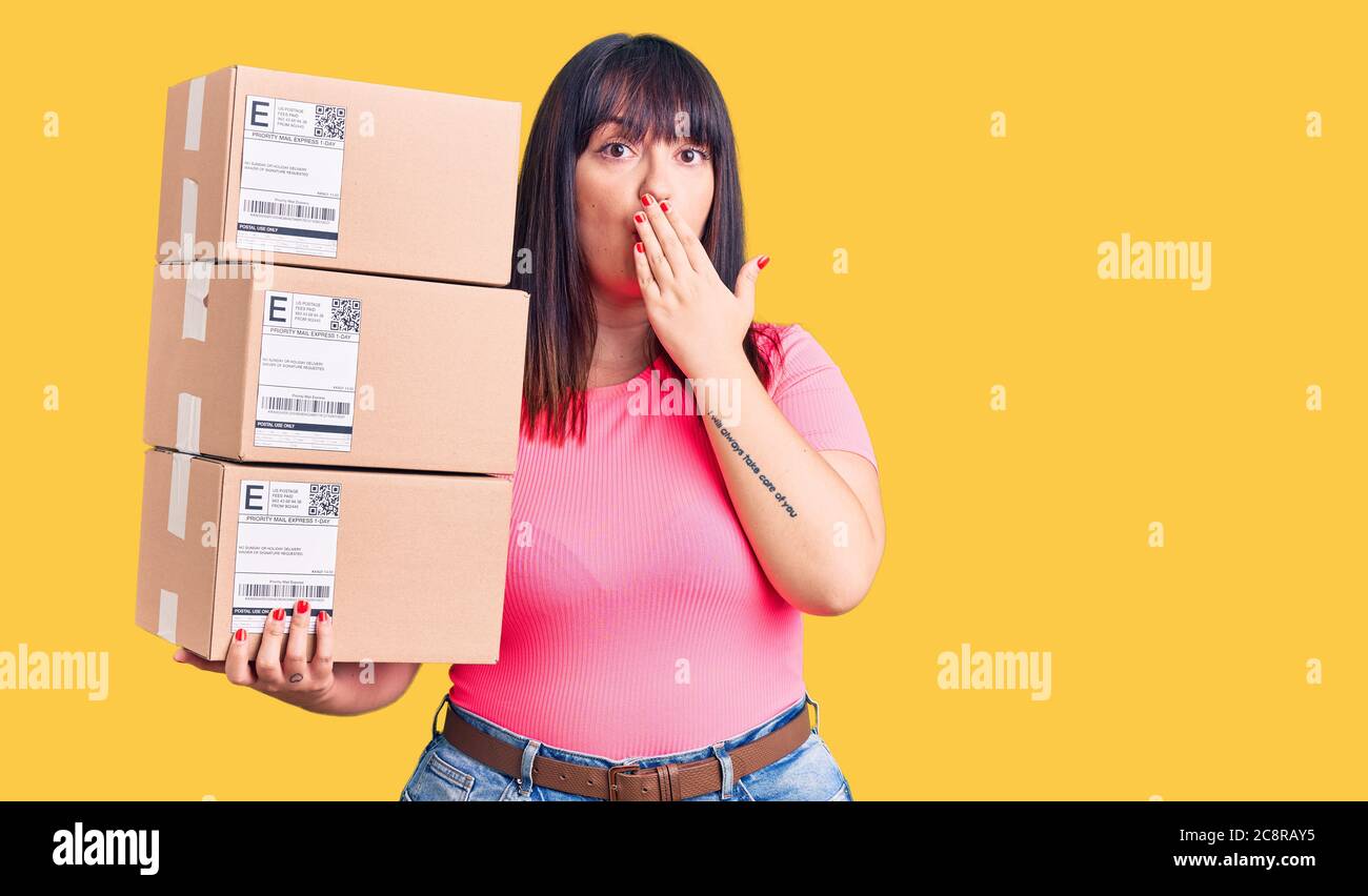 Young plus size woman holding delivery package covering mouth with hand ...