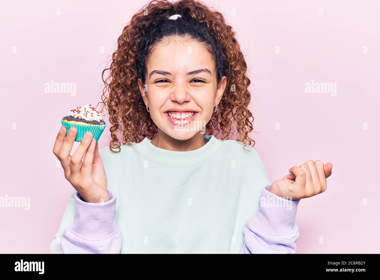 Beautiful kid girl with curly hair holding cupcake screaming proud ...