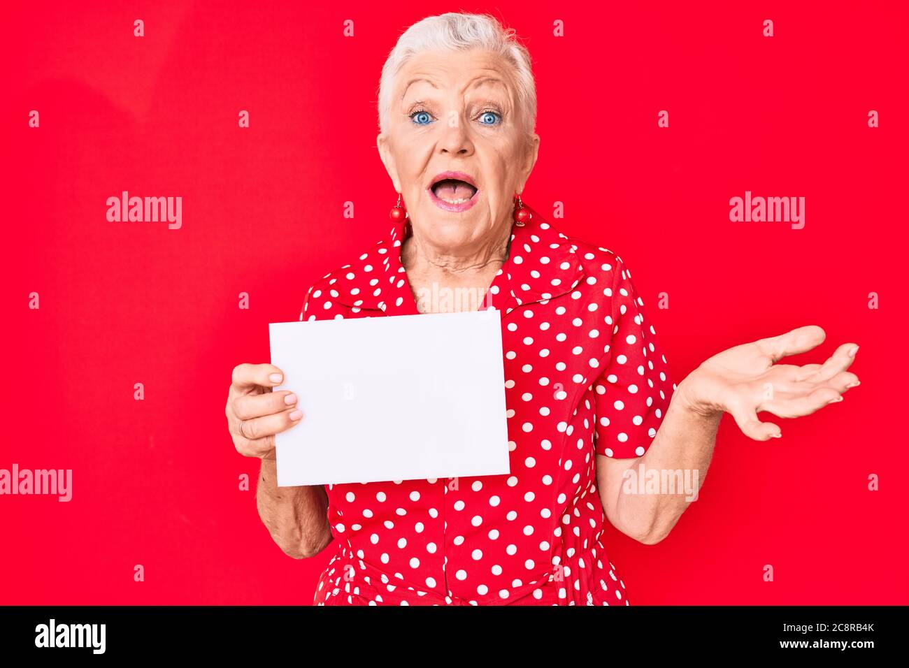 Senior beautiful woman with blue eyes and grey hair holding blank empty ...