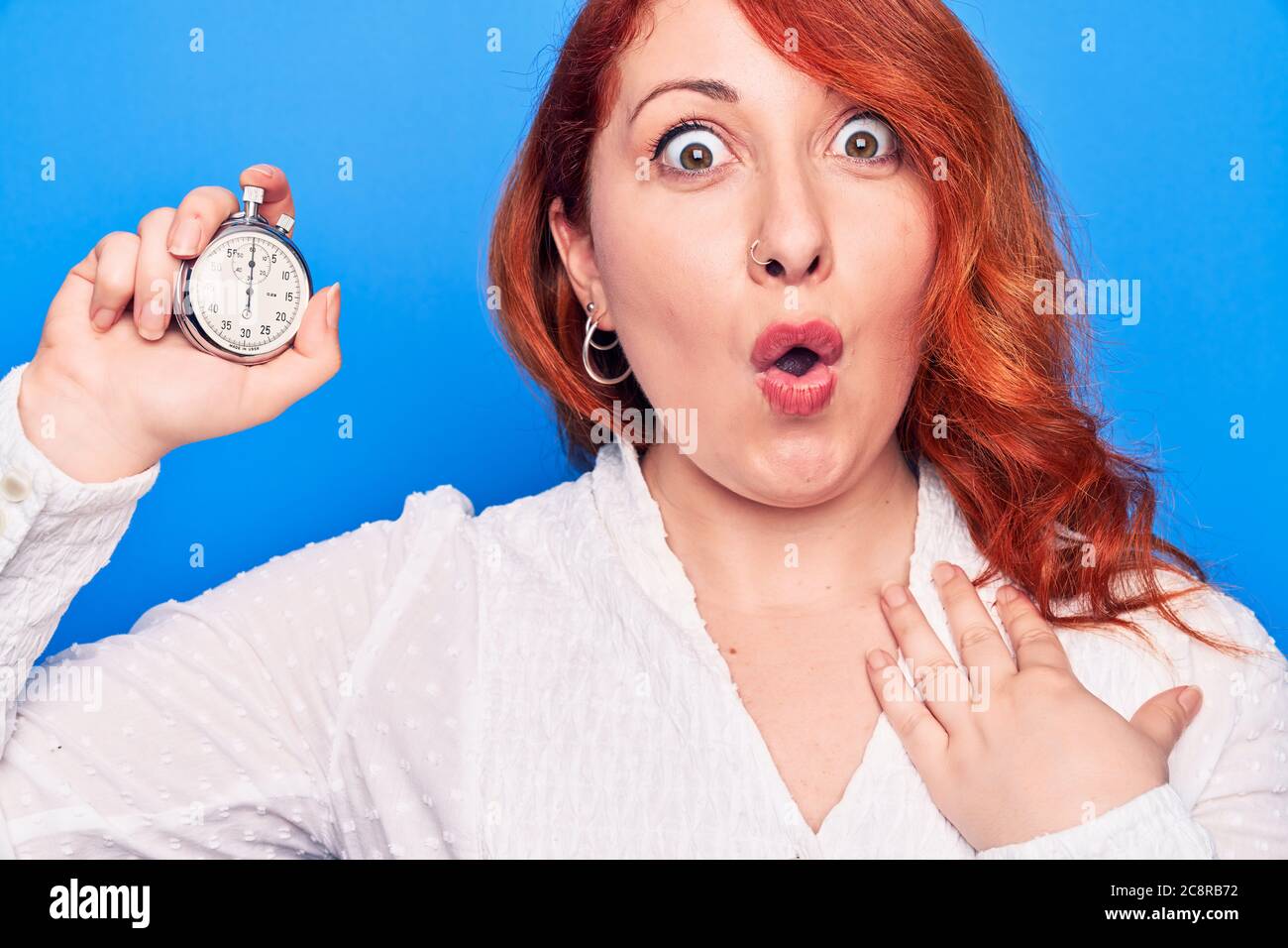 Young beautiful redhead woman doing countdown using stopwatch over blue ...